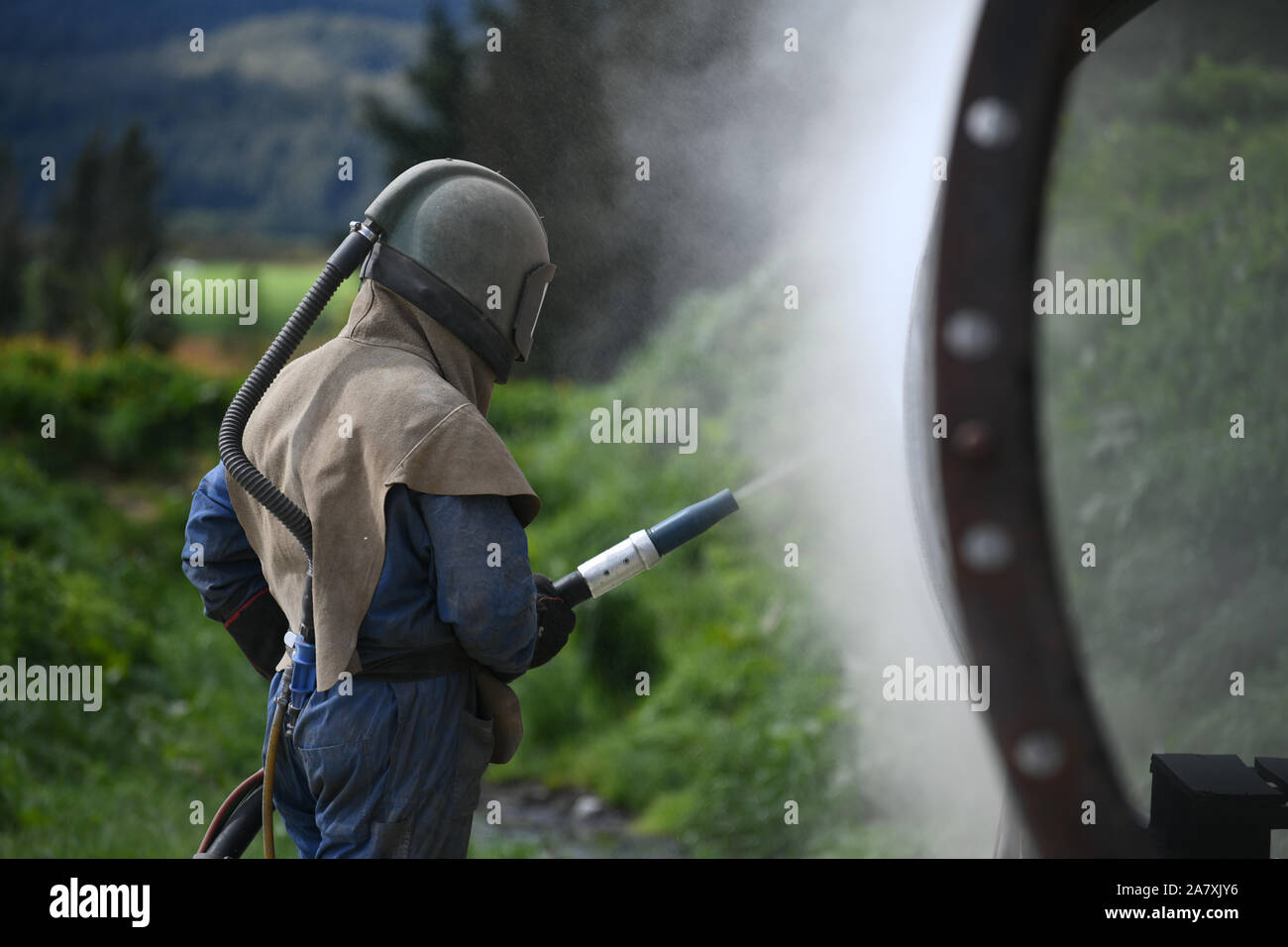 A man weating full safety gear sandblasts the steel casing of a meat ...