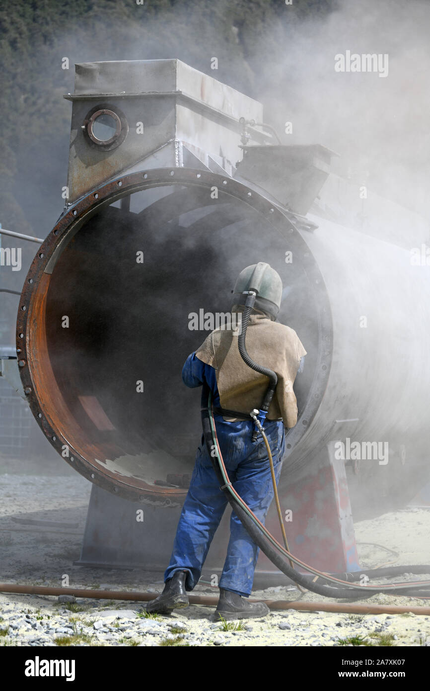 A man weating full safety gear uses ground glass to sandblast the steel ...