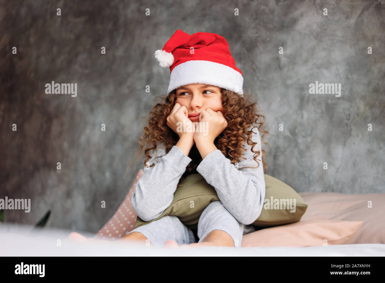 Curly haired beautiful tween girl in Santa hat and pajamas sitting on ...