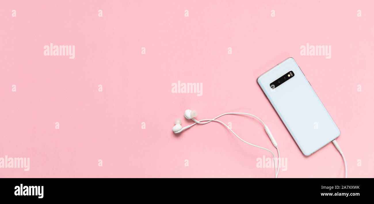 Mobile phone back view white color and earphones against pink color ...