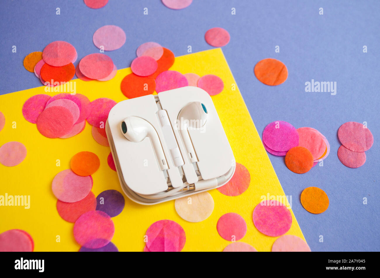 White earphones in a white plastic case on a bright yellow and purple ...