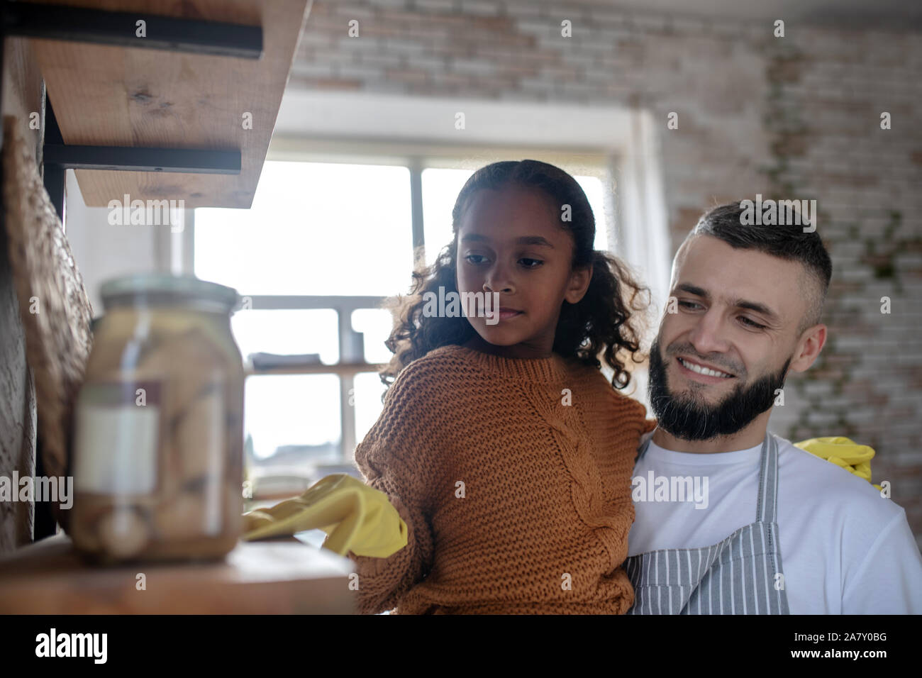 Bearded father smiling while daughter dusting shelves Stock Photo - Alamy