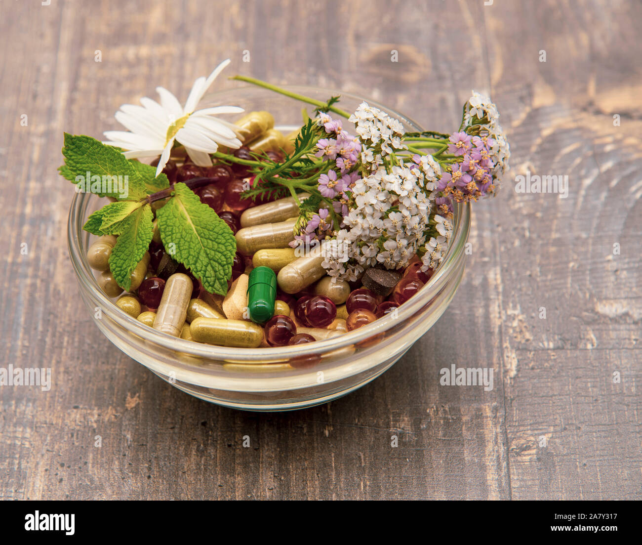 A bowl with various capsules and tablets, medicinal and aromatic herbs ...