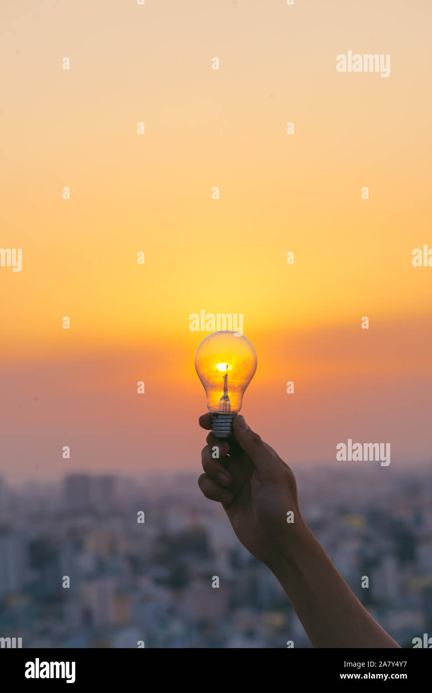 Hand hold a light bulb on sunset background for saving energy and ...