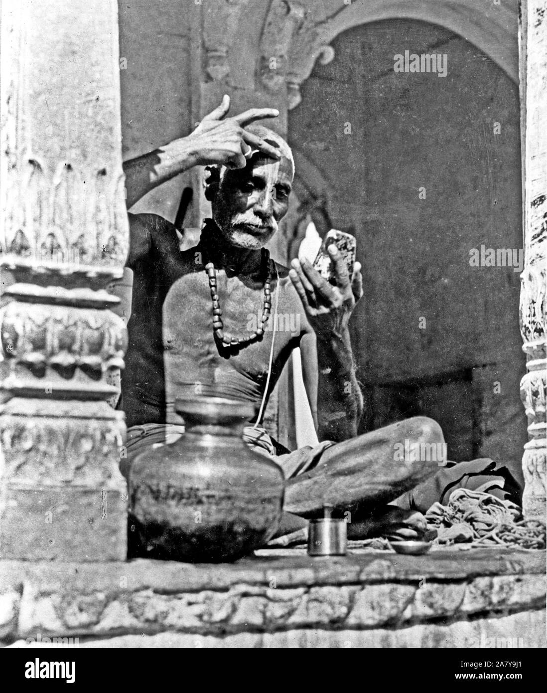 Brahman priest, in India, painting his forehead with the red and white ...