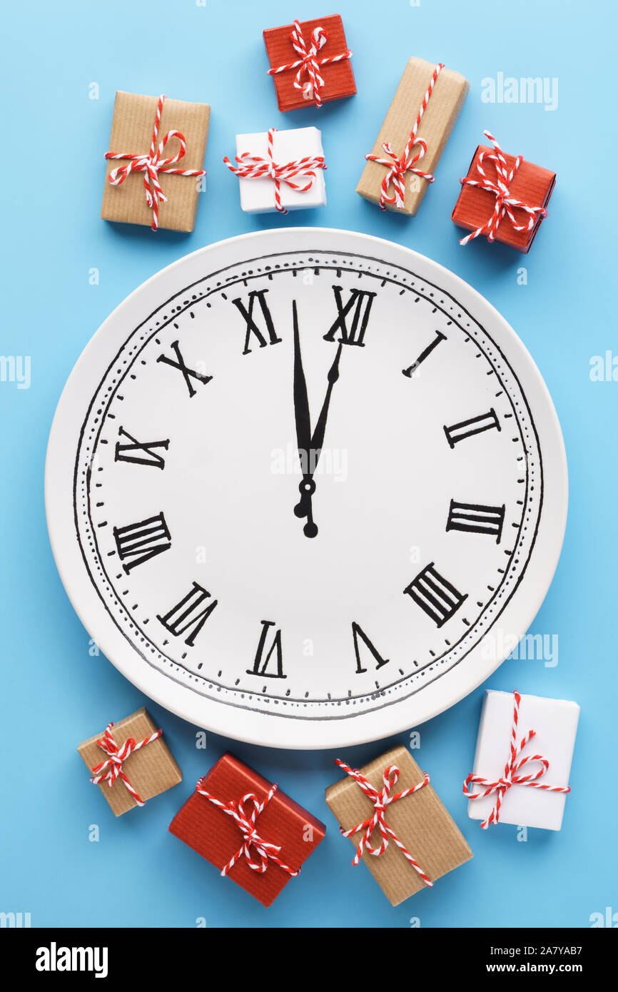 Gift boxes around a plate clock on light blue background. New Year or ...