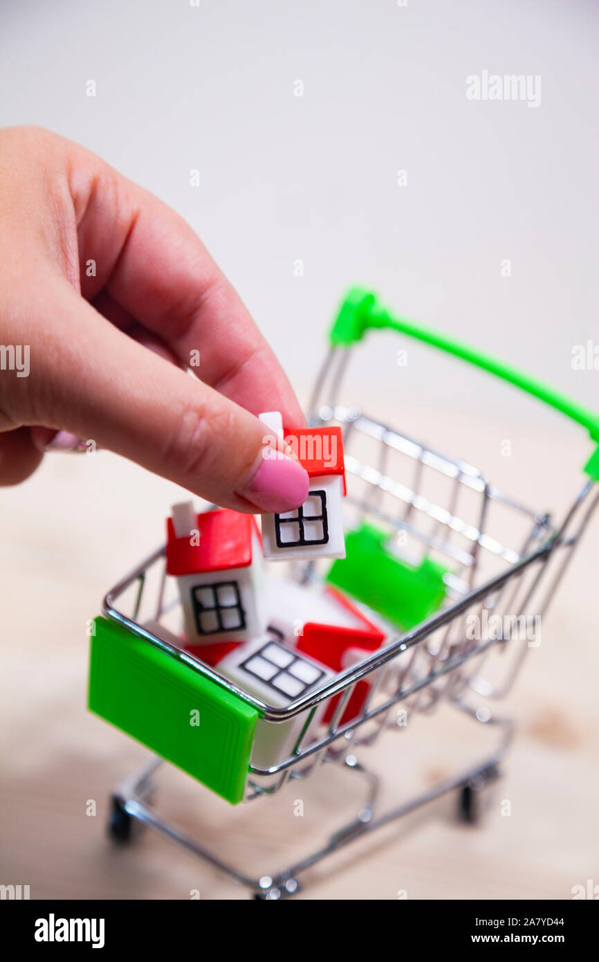 Female hand puts a house in a shopping cart. Concept: buying, selling ...