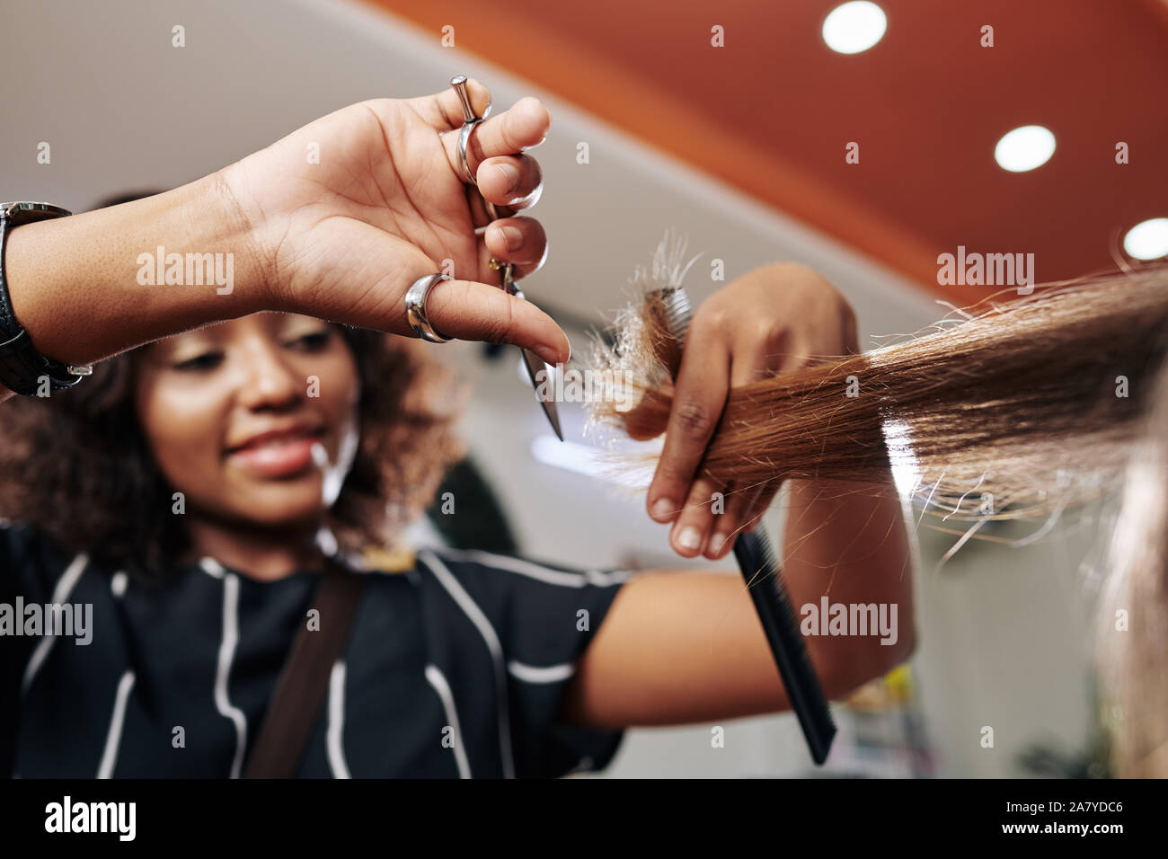 Close-up image of smiling hairdresser cutting split ends of section of ...