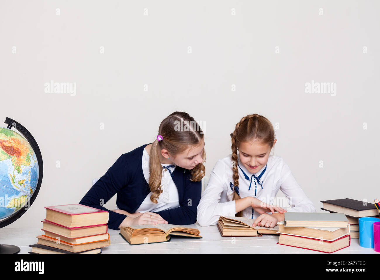 two schoolgirl girls with books and a globe in class at the desk Stock ...