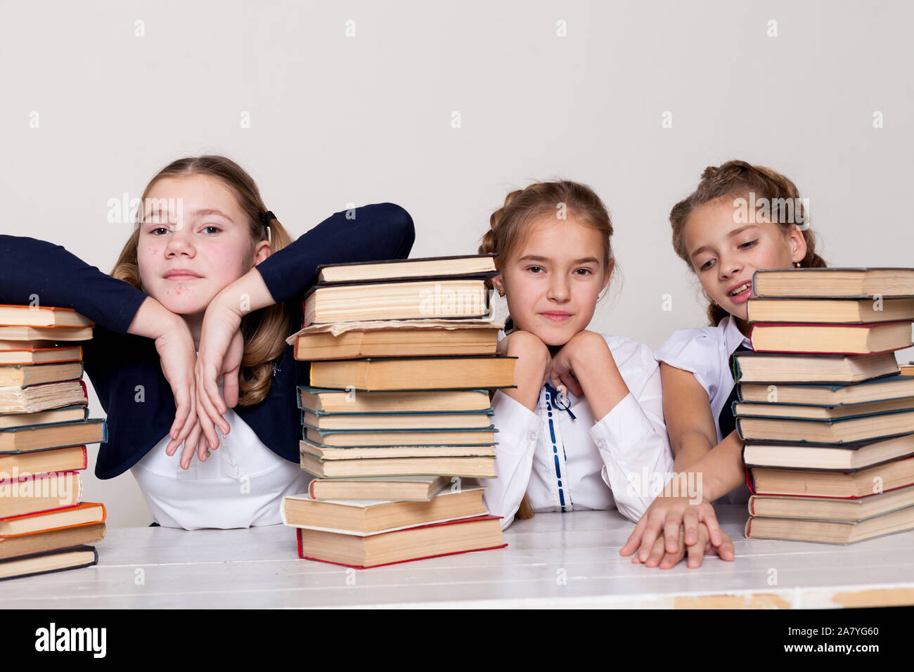 three schoolgirl girls with books in the library in class at the desk ...