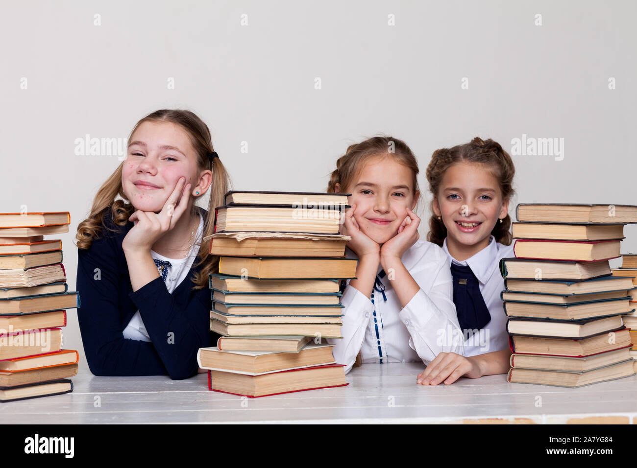 three schoolgirl girls with books in the library in class at the desk ...