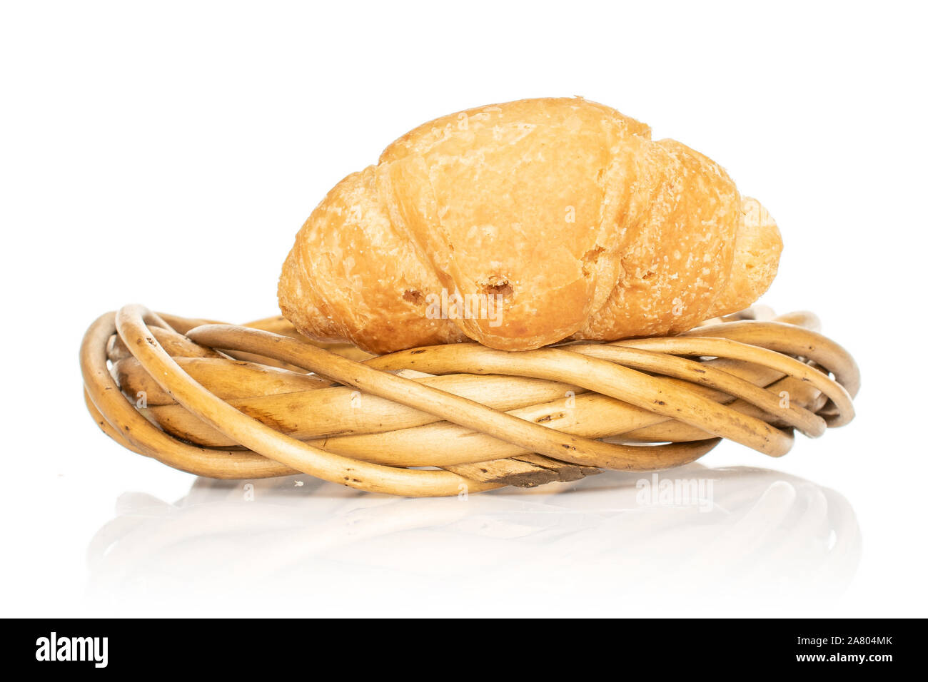 One whole fresh baked mini croissant in wicker vine circle isolated on ...
