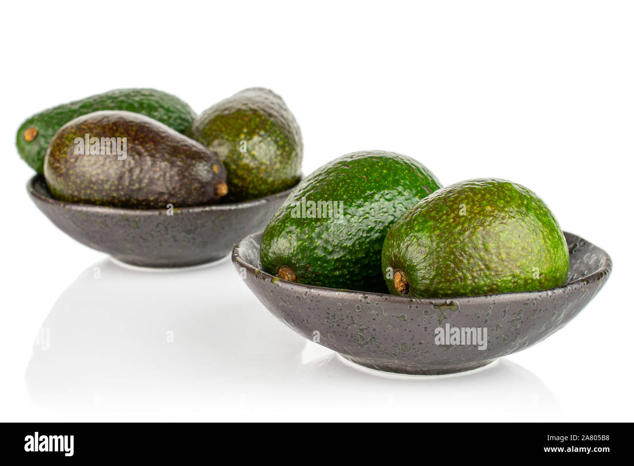 Group of five whole fresh green avocado in dark ceramic bowl isolated ...