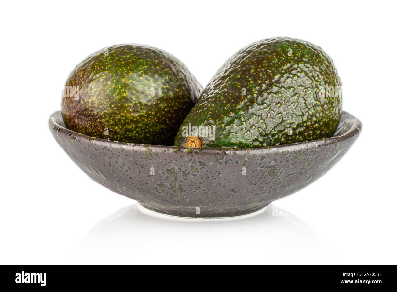 Group of two whole fresh green avocado in dark ceramic bowl isolated on ...