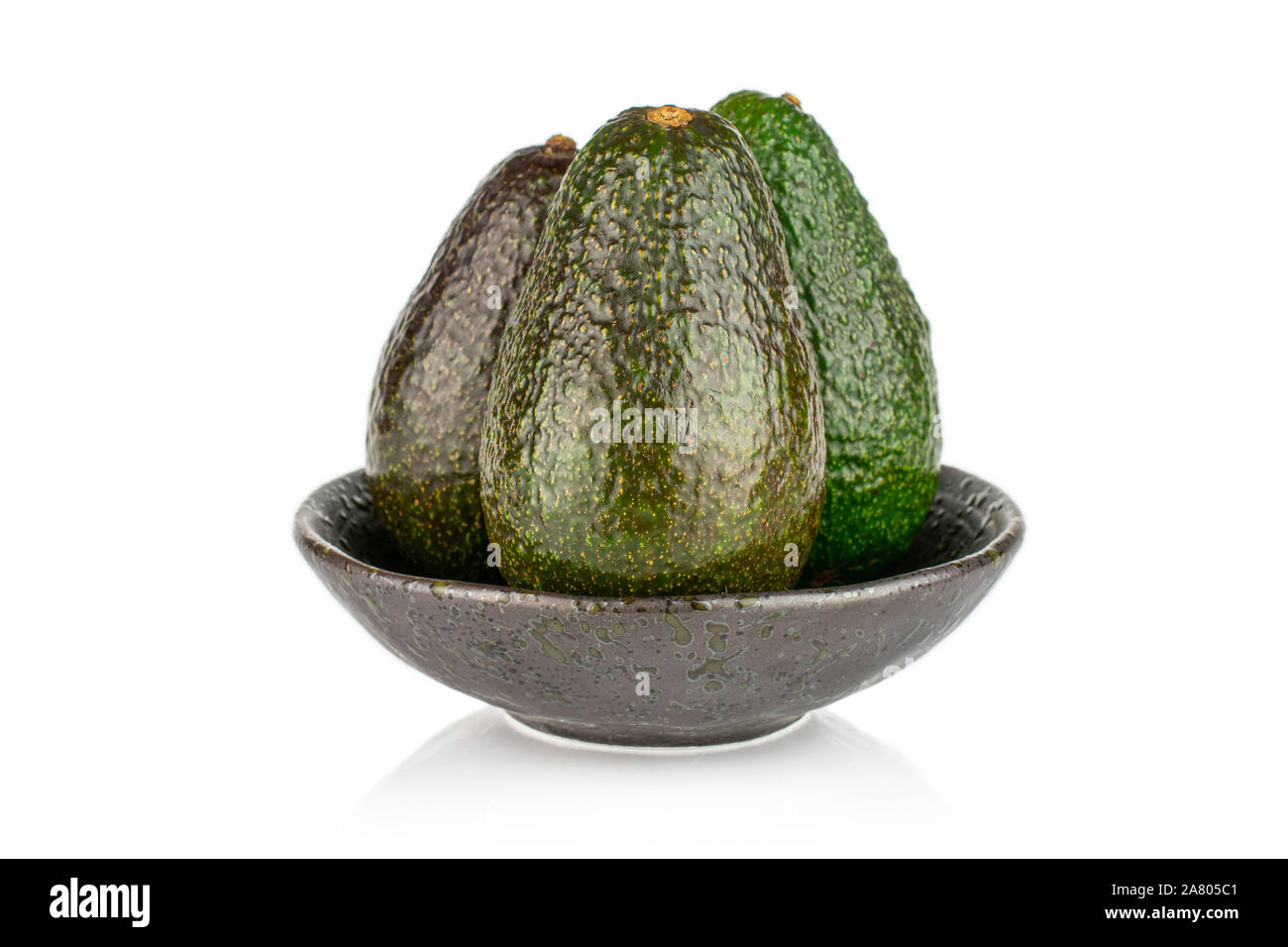 Group of three whole fresh green avocado in dark ceramic bowl isolated ...