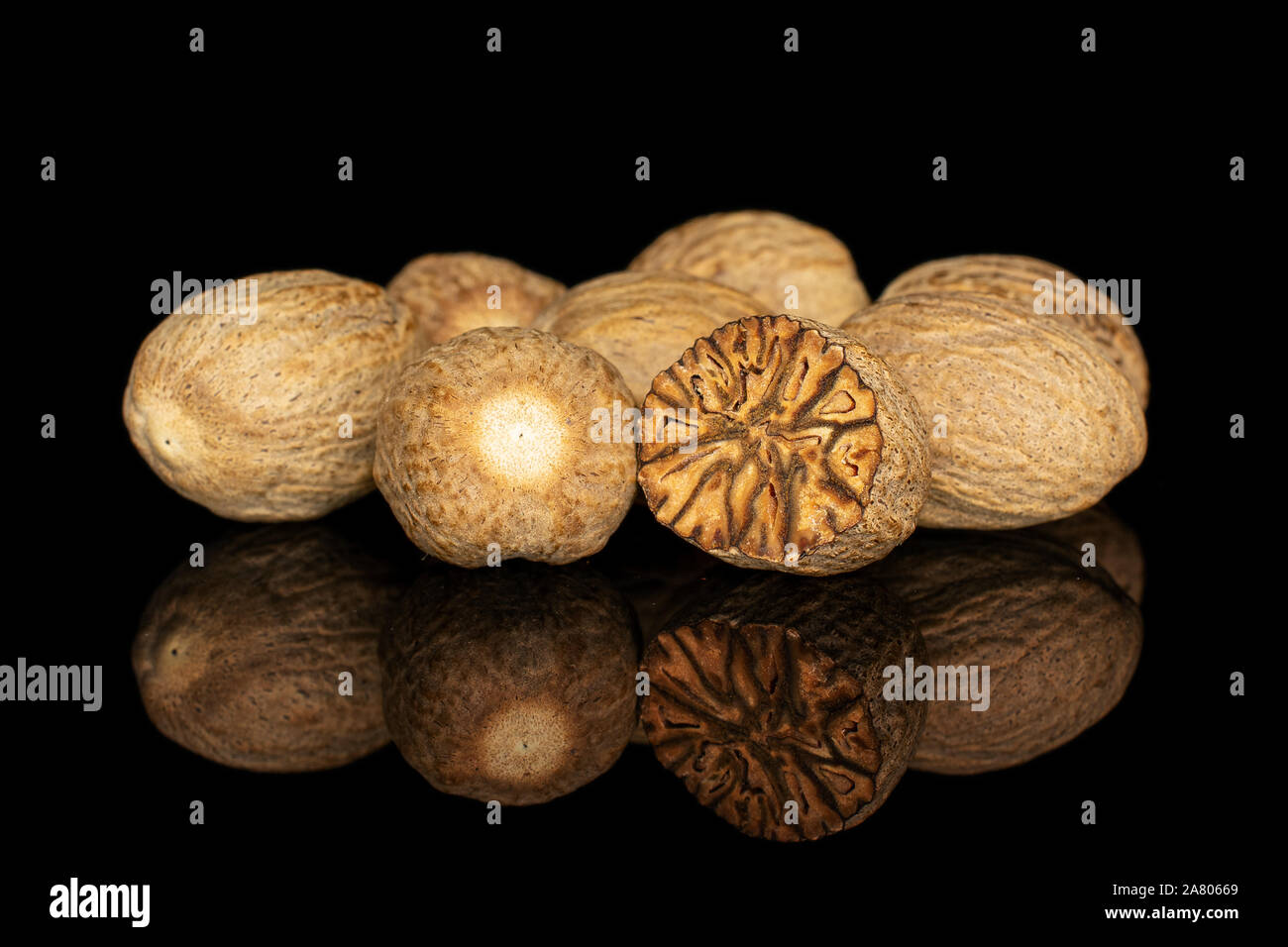 Group of six whole one half of dry brown nutmeg isolated on black glass ...