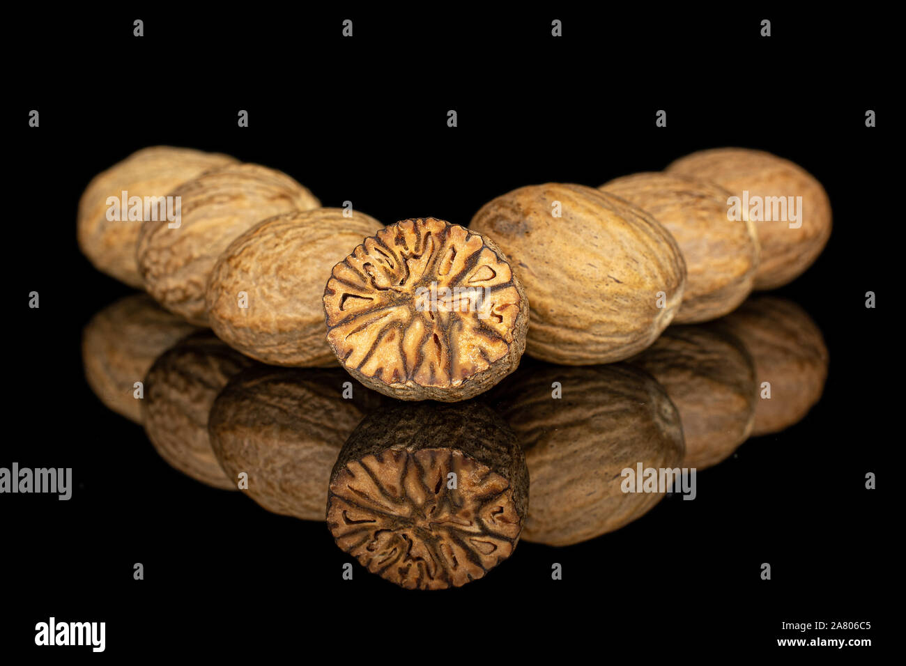 Group of six whole one half of dry brown nutmeg isolated on black glass ...
