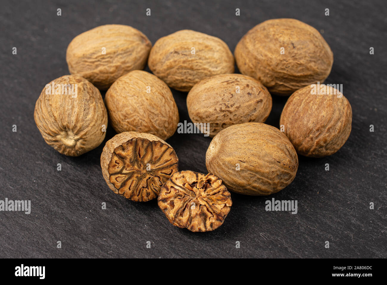Group of eight whole one half one piece of dry brown nutmeg on grey ...