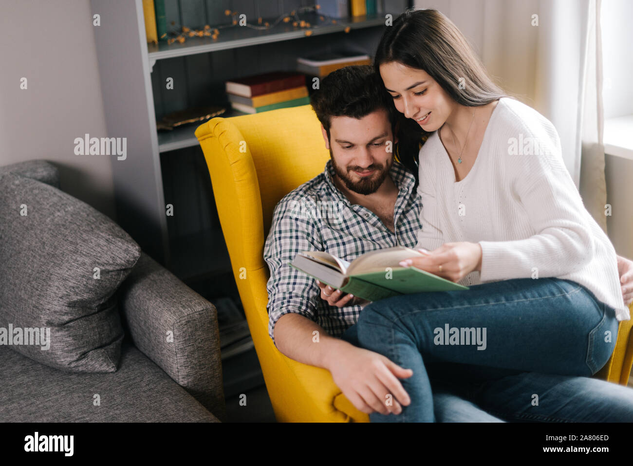 Lovely positive young couple reading a book together, sitting on yellow ...