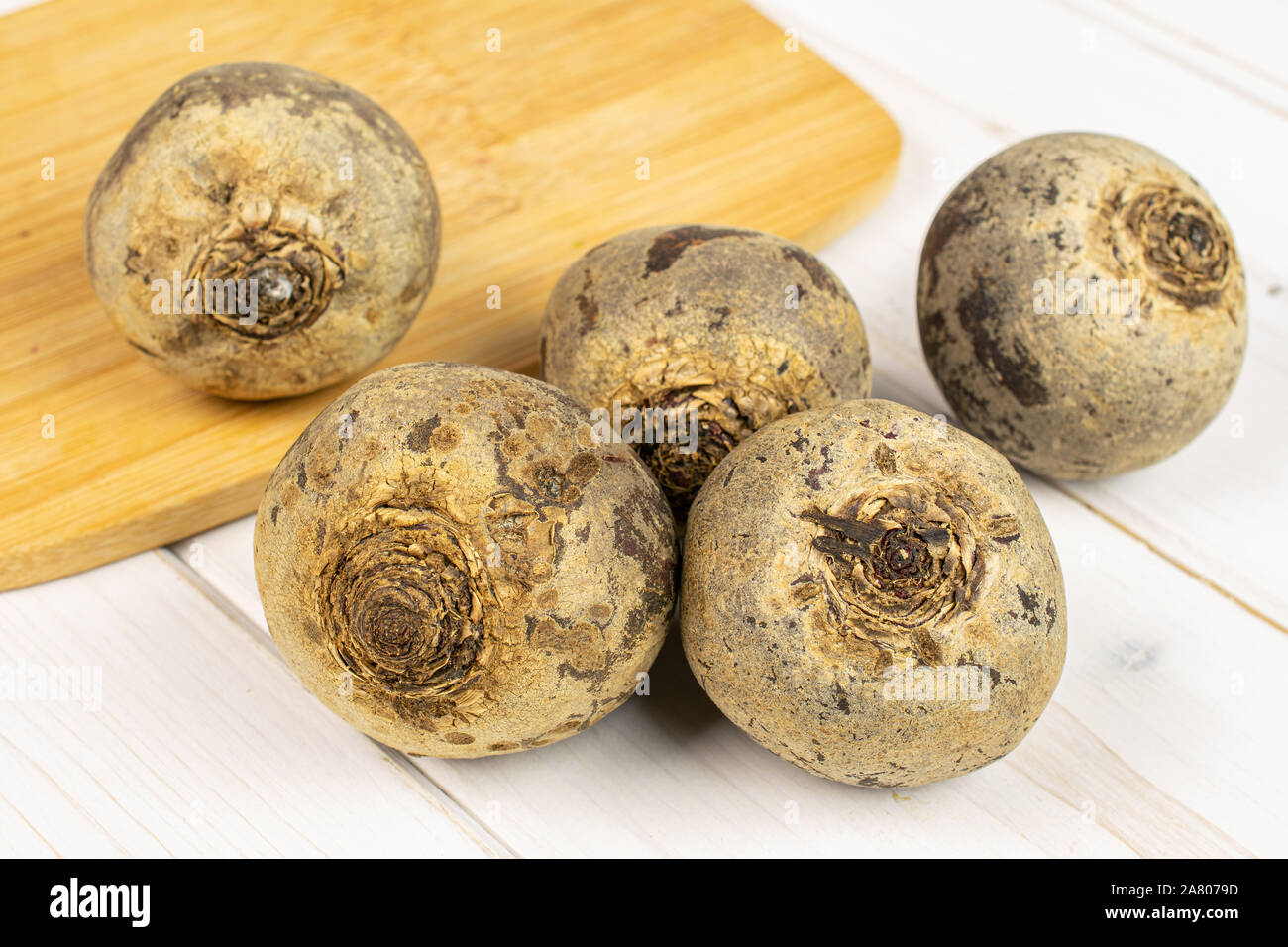 Group of five whole raw red beetroot on bamboo cutting board on white ...
