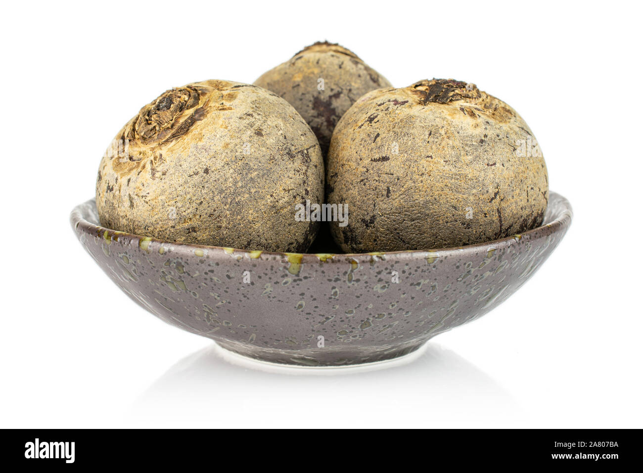 Group of three whole raw red beetroot in dark ceramic bowl isolated on ...