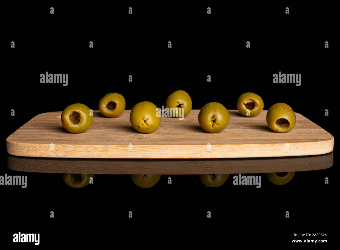Group of seven whole pitted green olive on bamboo cutting board ...
