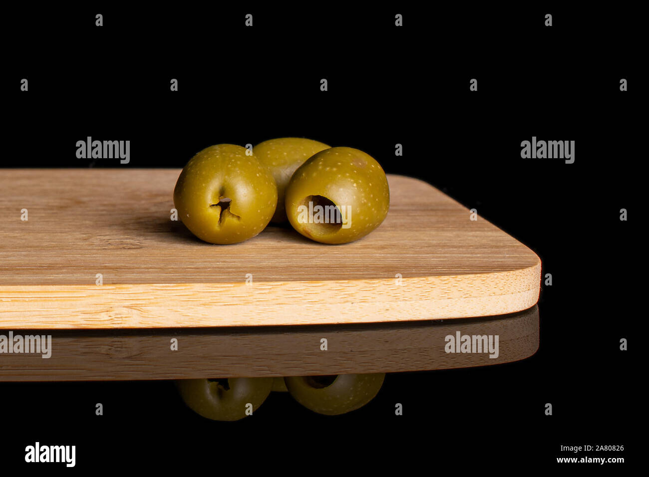Group of three whole pitted green olive on bamboo cutting board ...