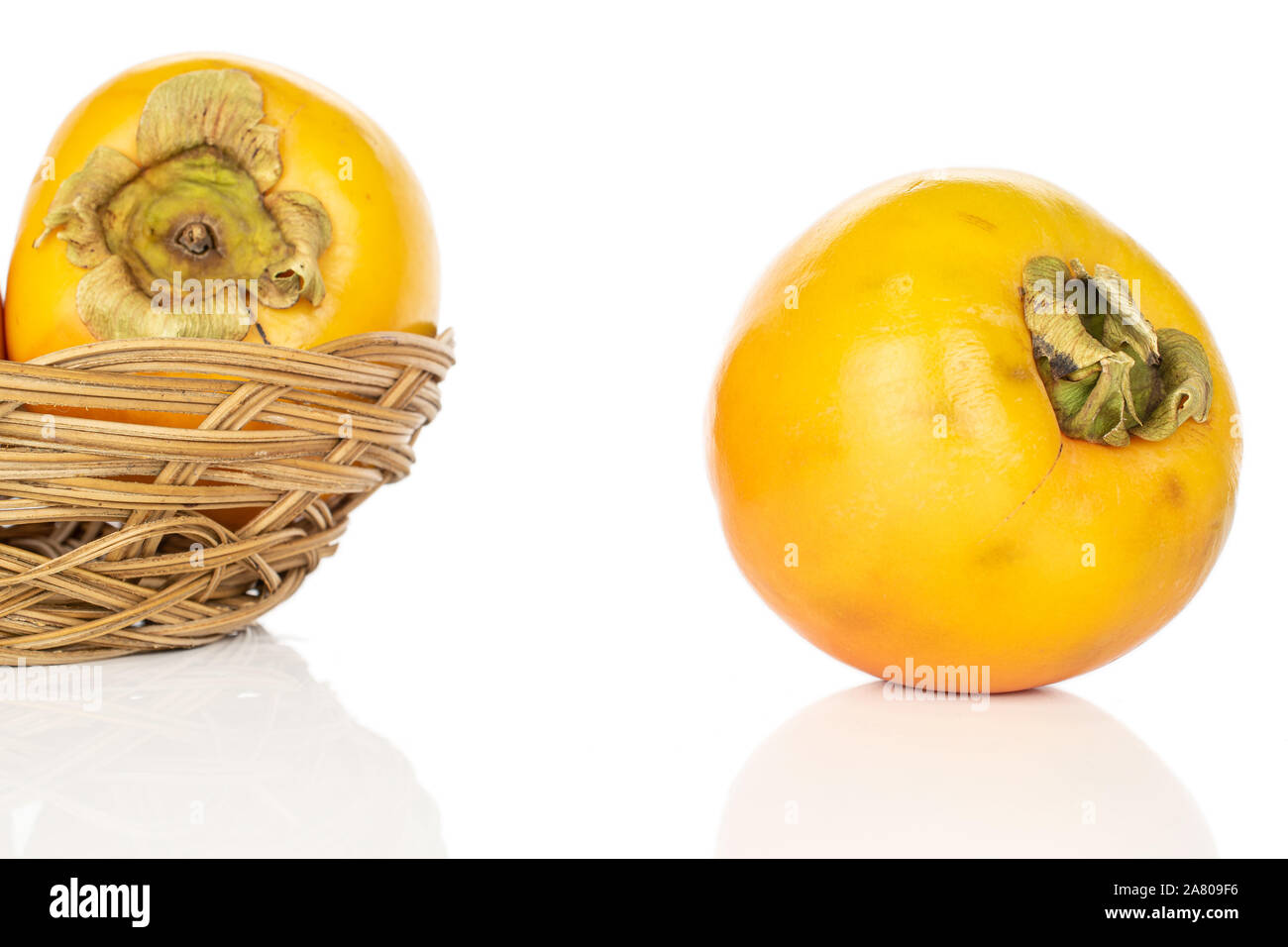 Group of two whole sweet orange persimmon in round rattan bowl isolated ...