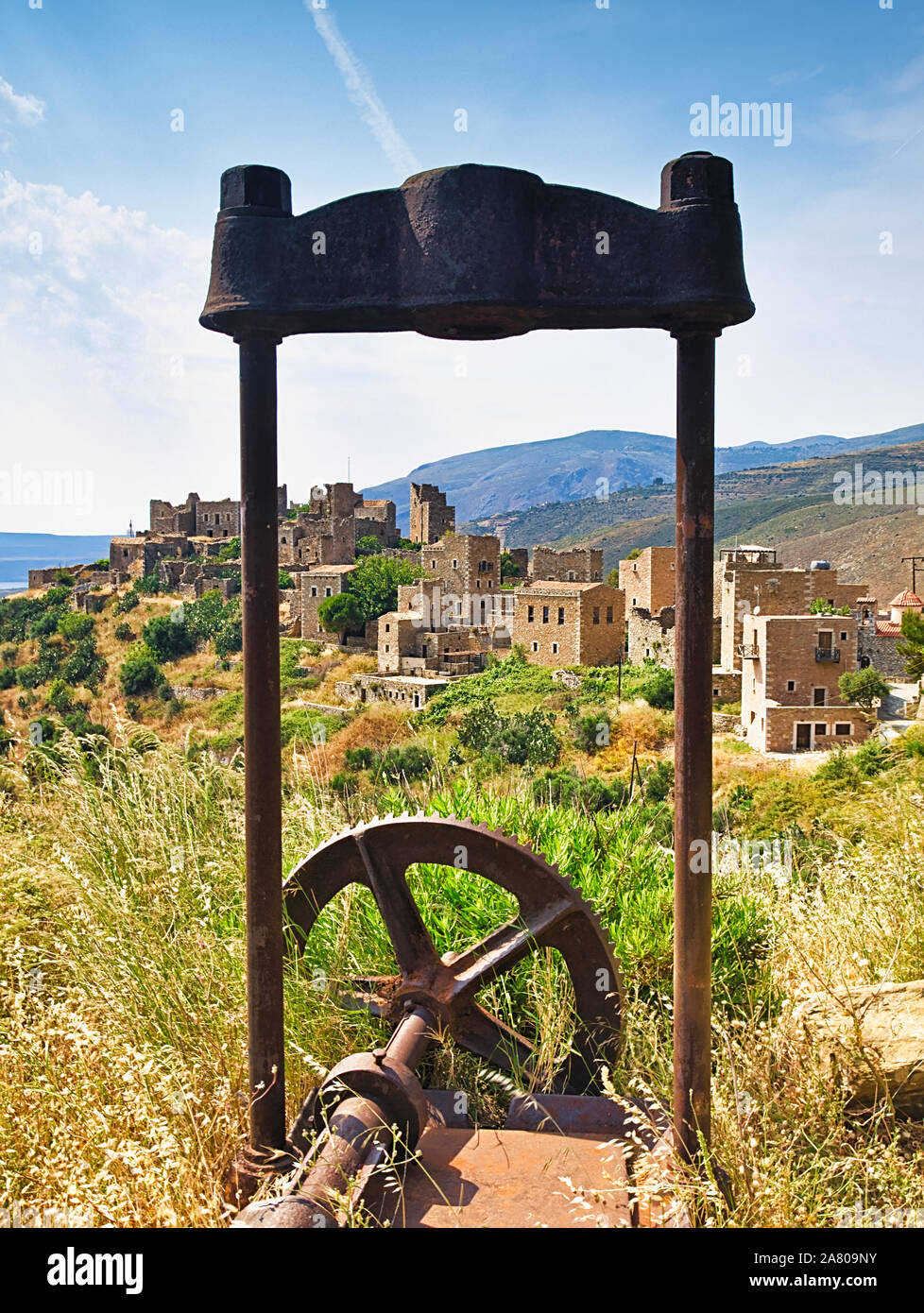 Old rusty mechanism with large gear and the medieval village of Vathia ...