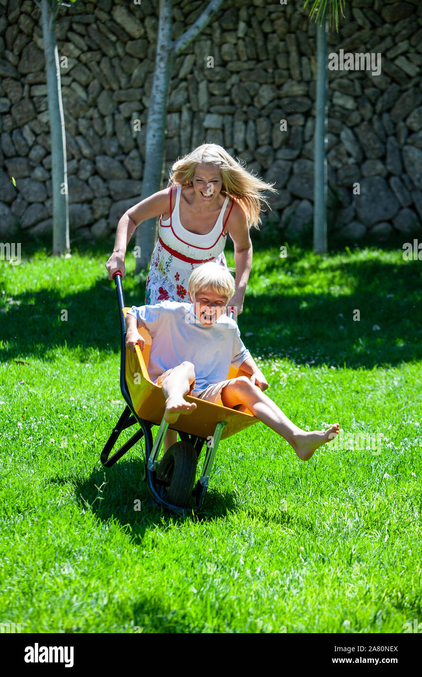 Mother pushing her son in the garden in a wheelbarrow Stock Photo - Alamy