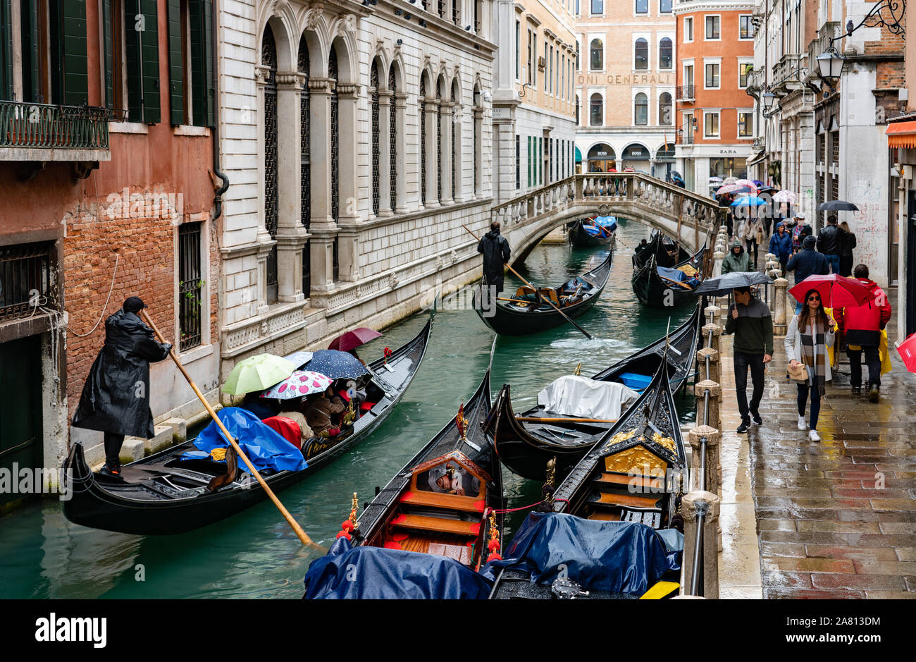 Rainy day in Venice with gondoliers rowing tourists along the canals ...