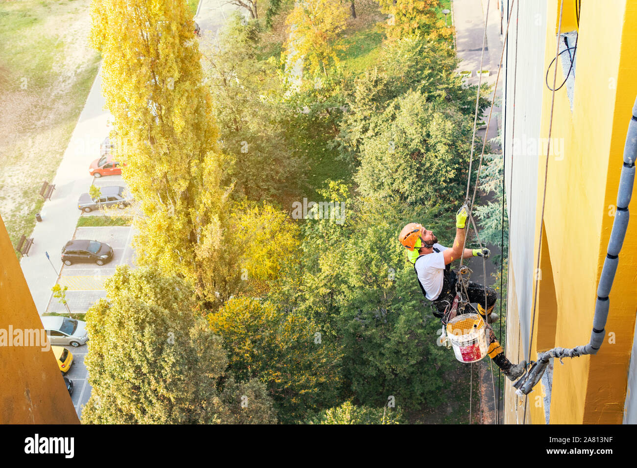 Industrial rope access worker hanging from the building while painting ...