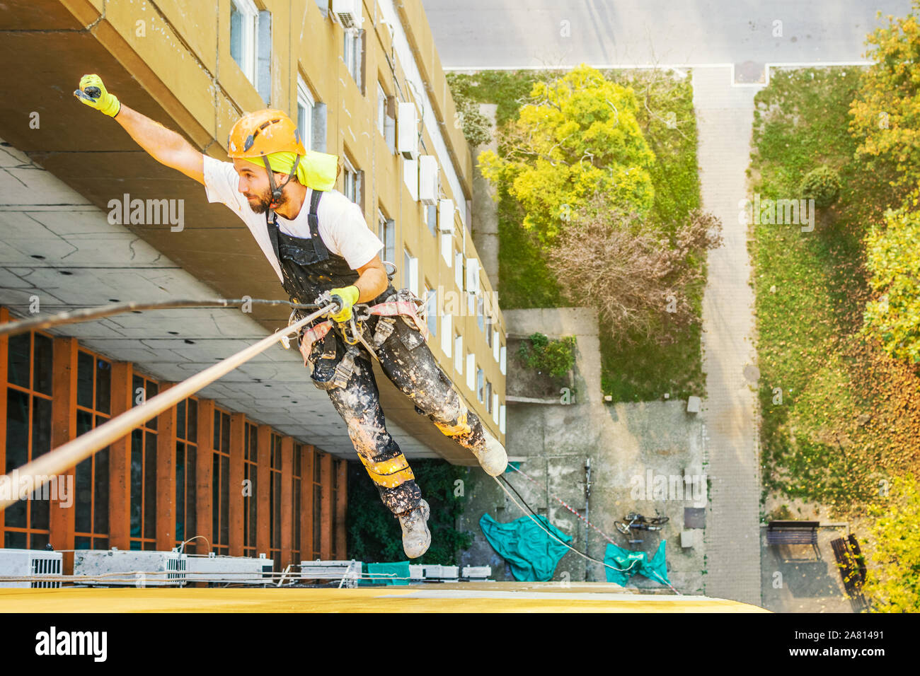 Industrial rope access worker hanging from the building while painting ...