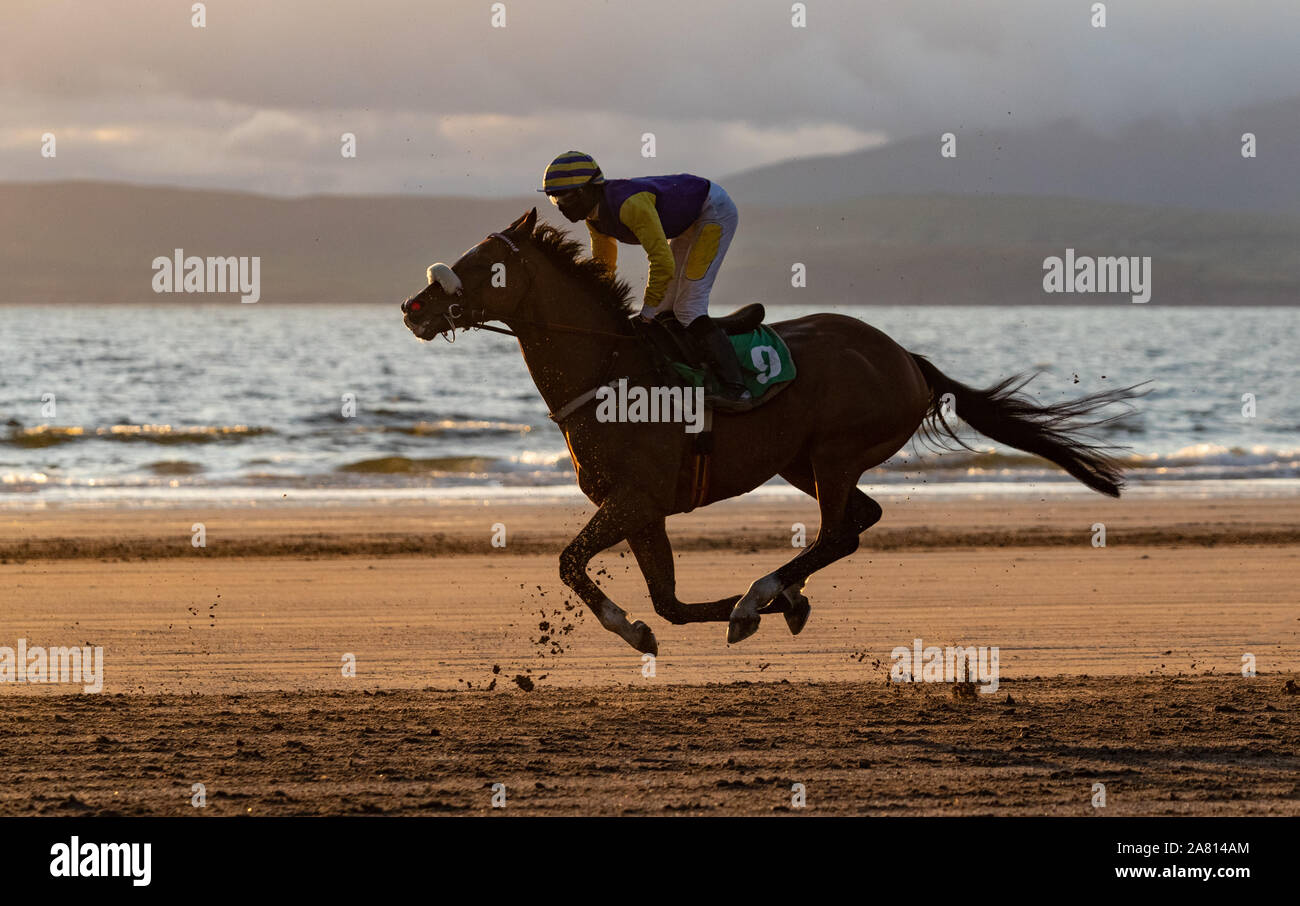 Race horse and jockey galloping on the beach at sunset on the west ...