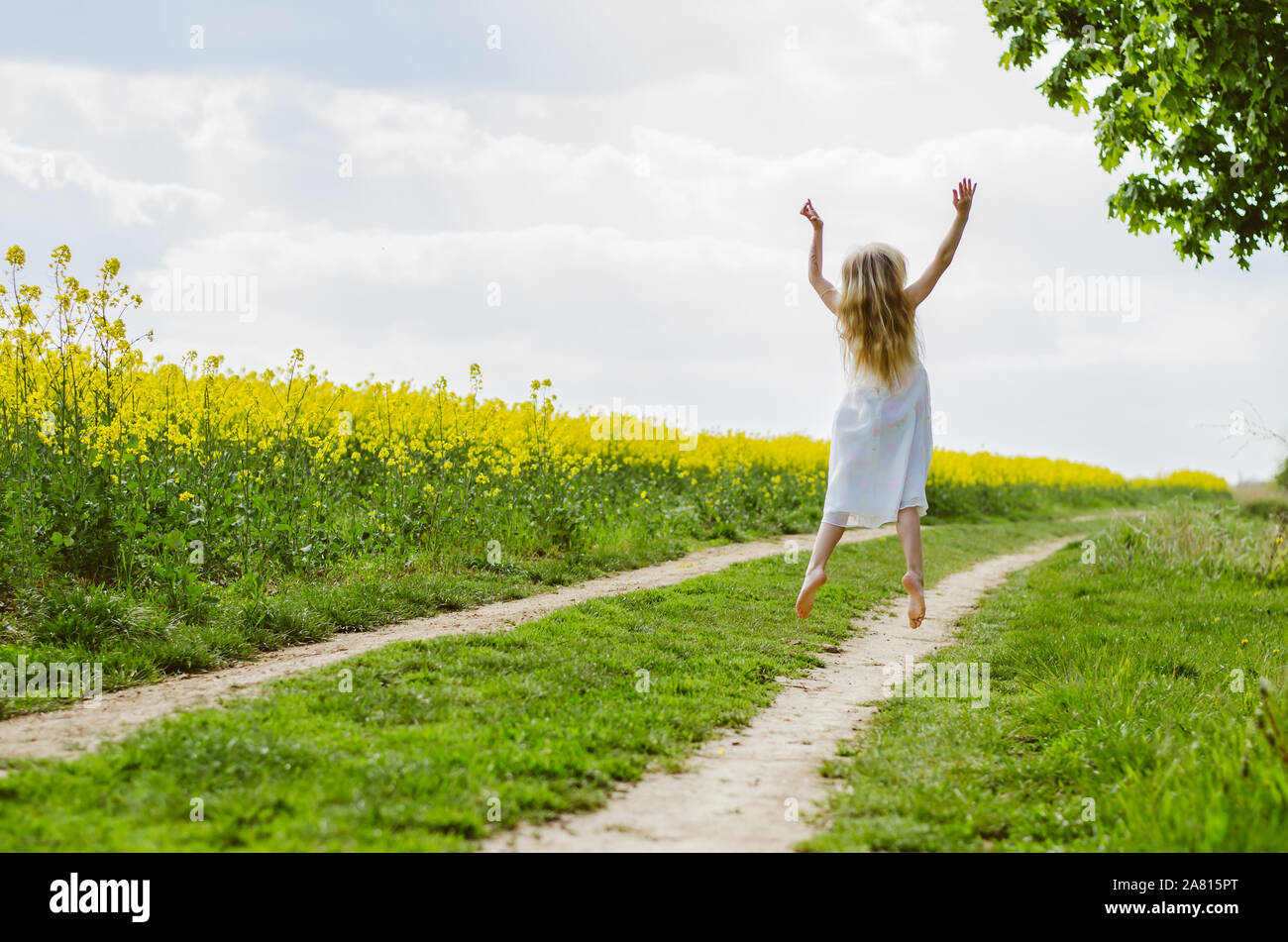 jumping figure of little girl in white long dress in green spring ...