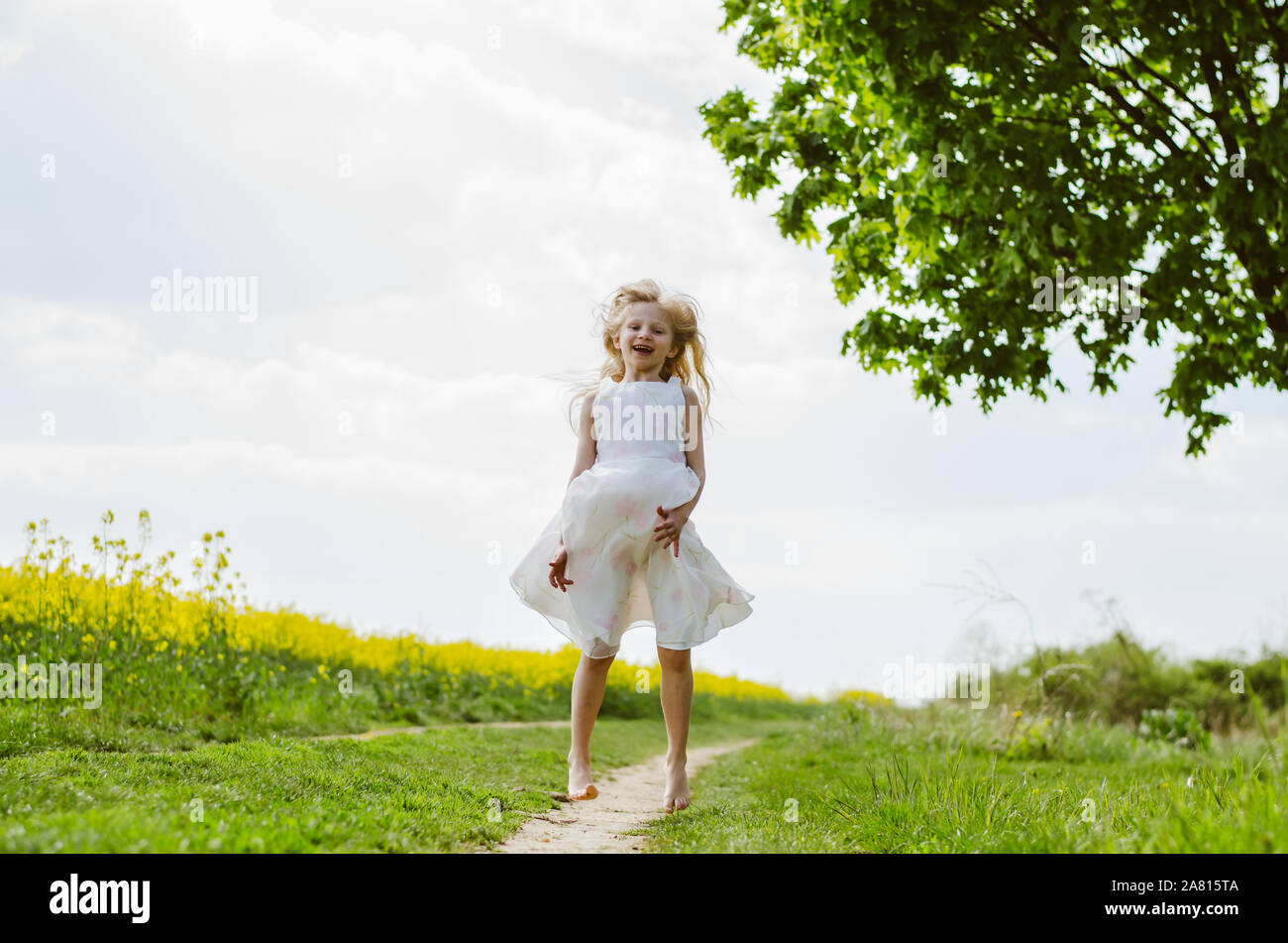 jumping figure of little girl in white long dress in green spring ...