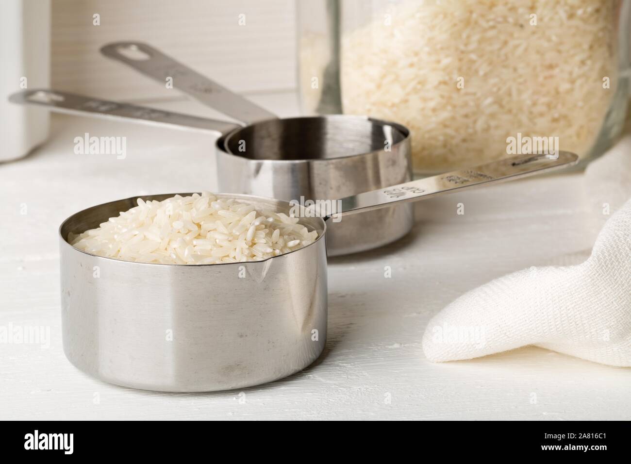 White uncooked, raw long grain rice in metal measurement scoop with ...