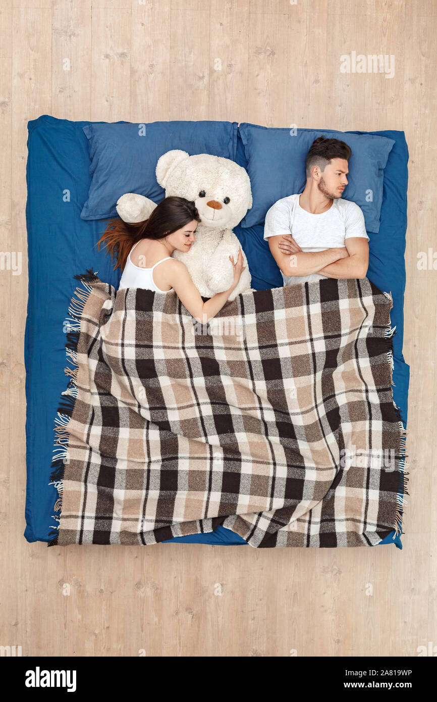 Bedtime. Young woman hugging teddy happy while man crossing arms ...