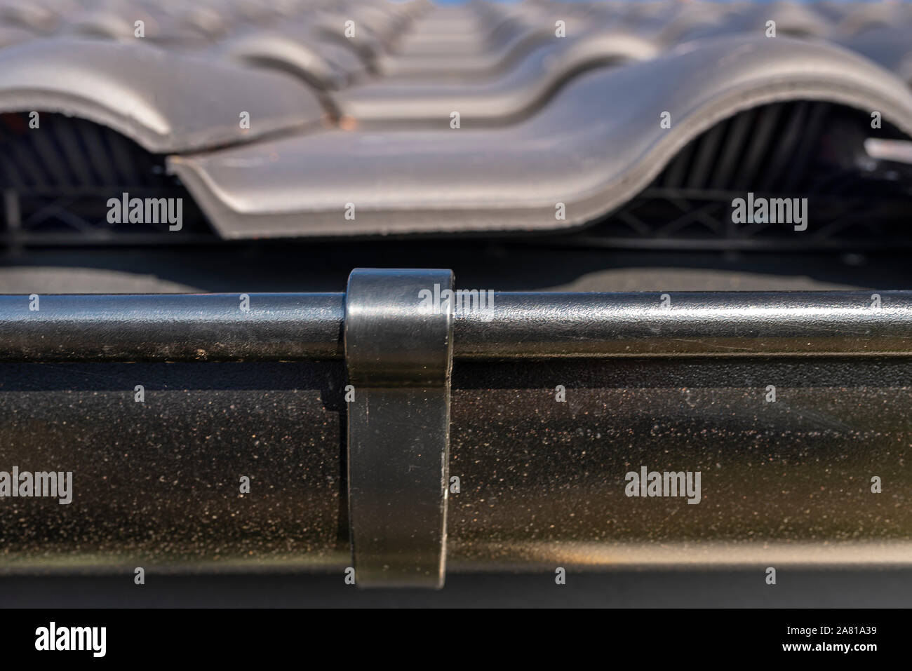 A metal, black gutter on a roof covered with ceramic tiles. Close up ...