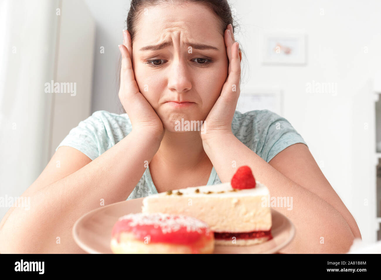 Junk Food. Chubby girl sitting at kitchen looking at plate with cake ...
