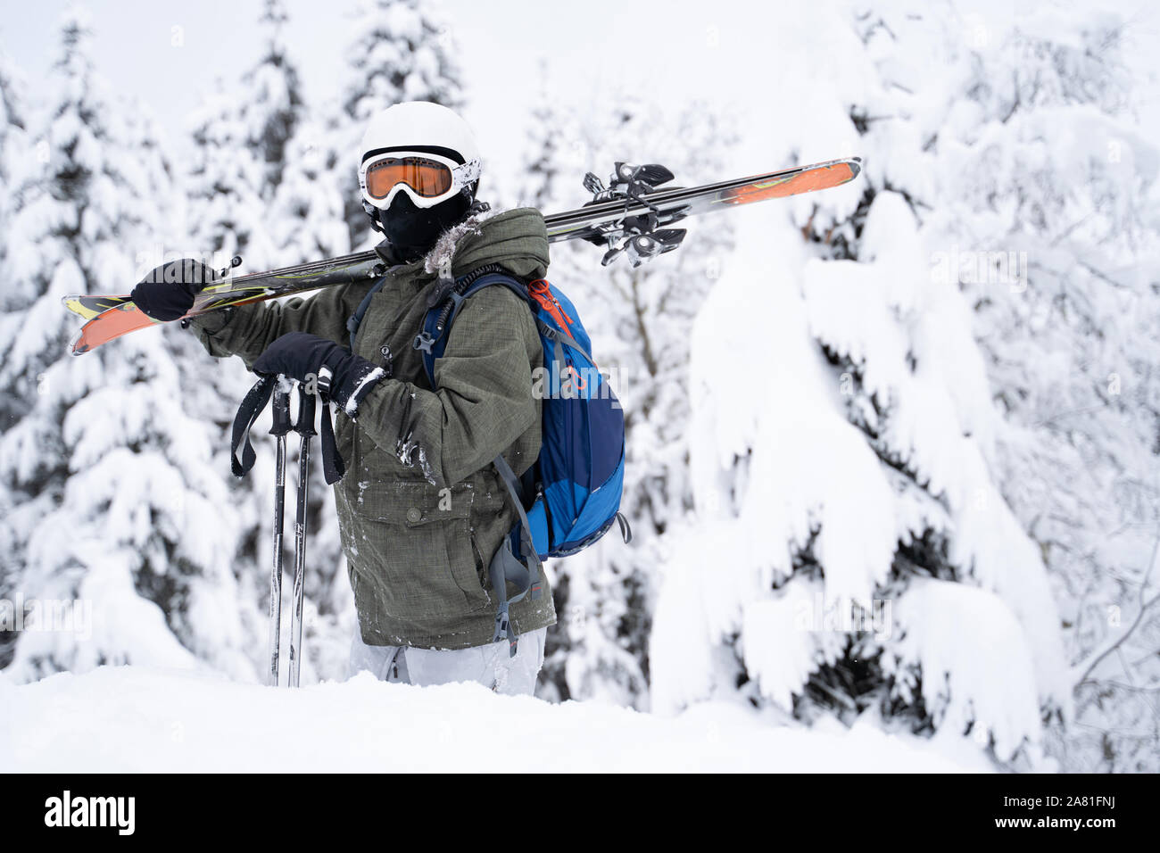 Image of athlete in helmet and mask with skis on his shoulder against ...