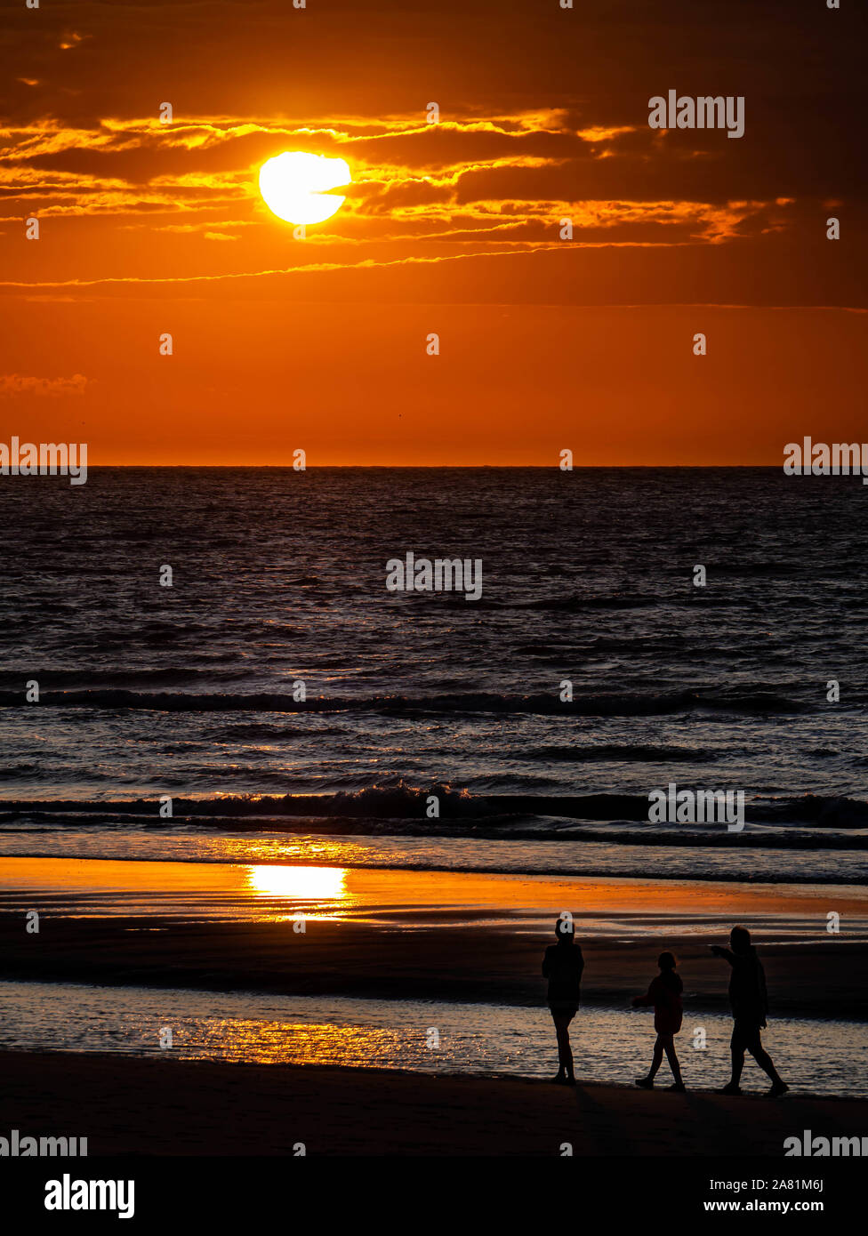 Young family enjoying a colorful sunset at the beach with the sun ...