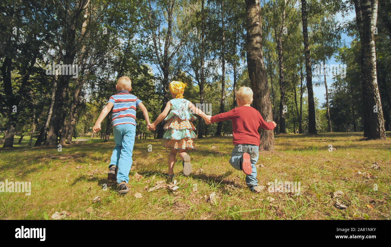 Three cheerful children are holding hands running in the park Stock ...
