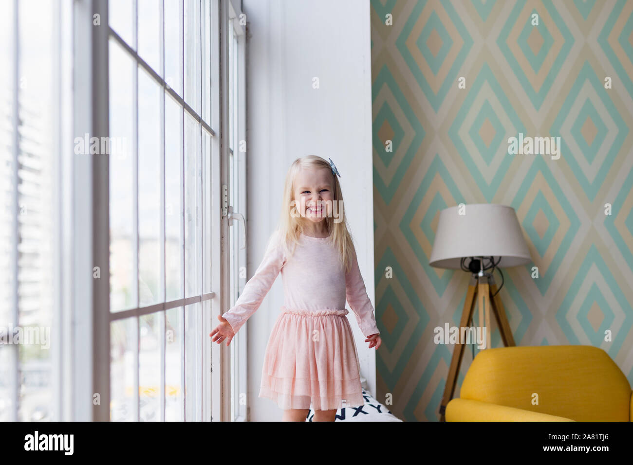 Happy little girl smiling while standing in front of window Stock Photo ...