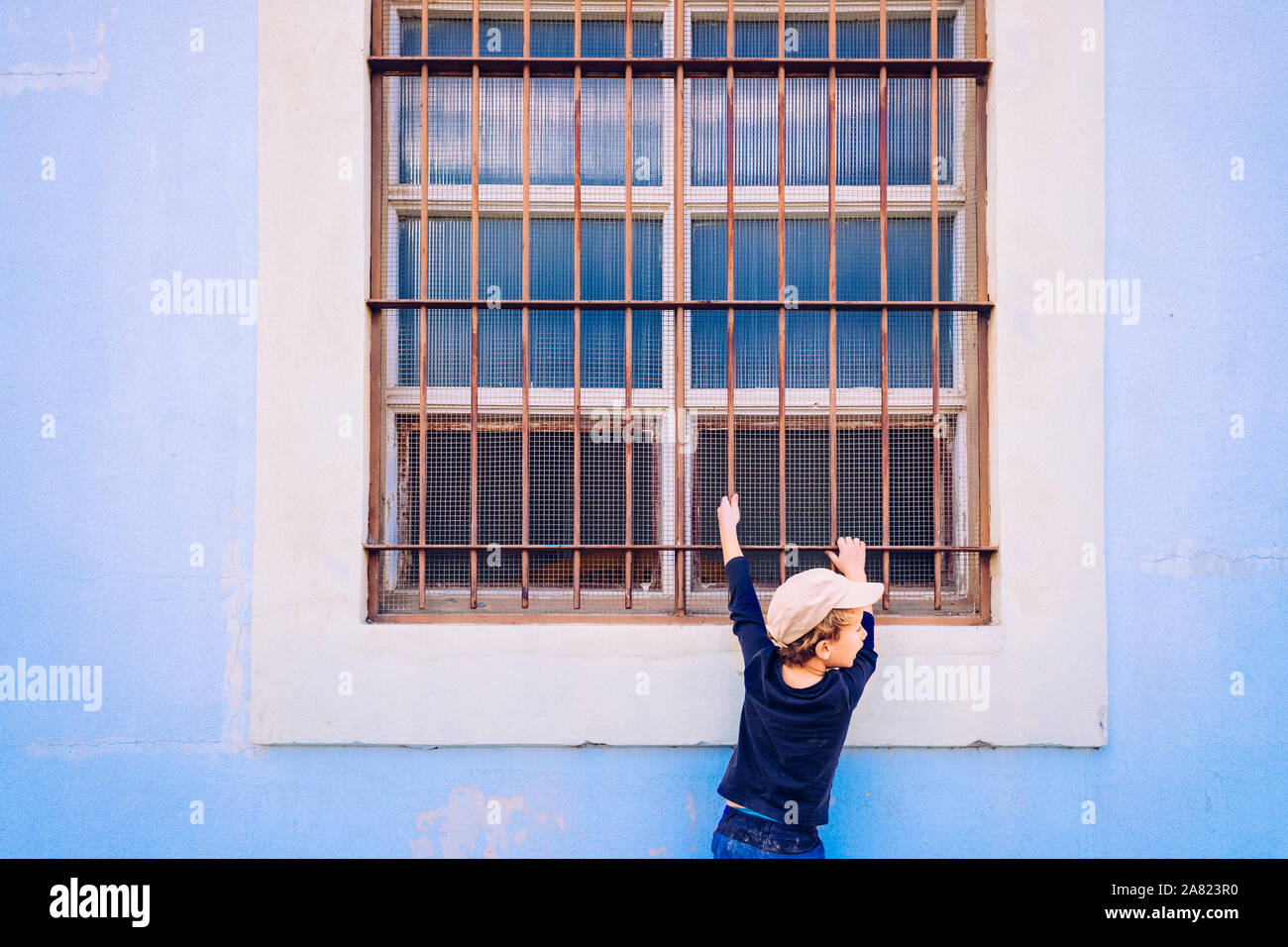 Boy playing climbing to the bars of a window in a blue wall Stock Photo ...