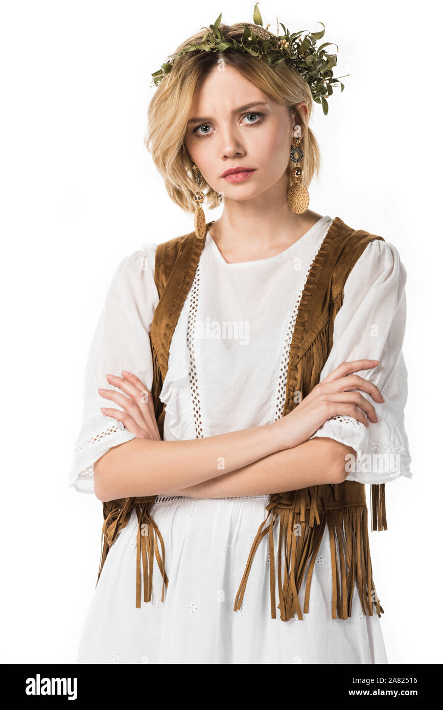 sad hippie girl in wreath looking at camera with folded arms isolated ...