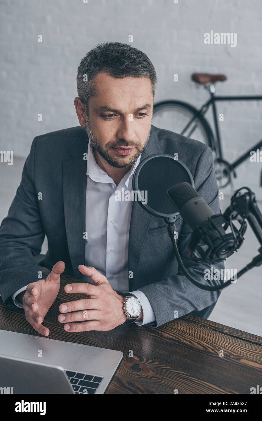 serious radio host gesturing while speaking in microphone at workplace ...