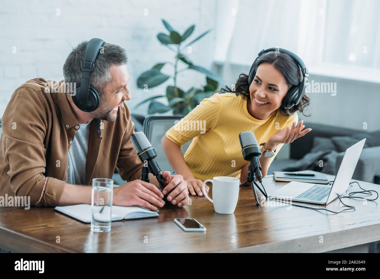 two radio hosts in headphones laughing while recording podcast in ...