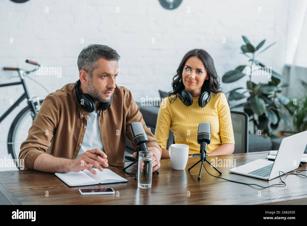 pretty radio host looking at camera while sitting at workplace near ...