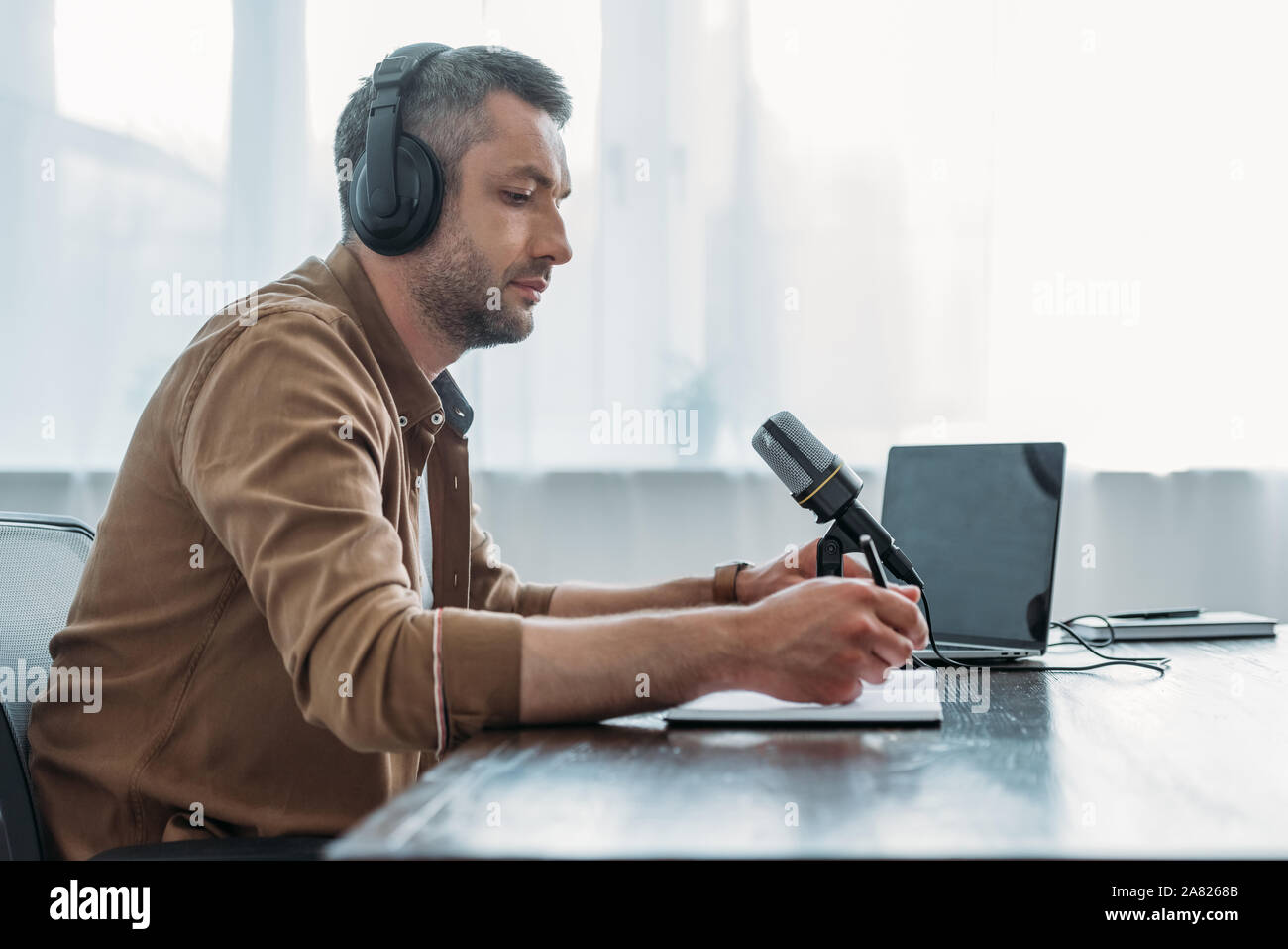 serious radio host in headphones sitting near microphone in ...